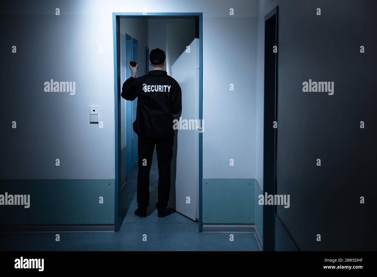 Rear View Of Male Security Guard With Flashlight Standing In Corridor ...
