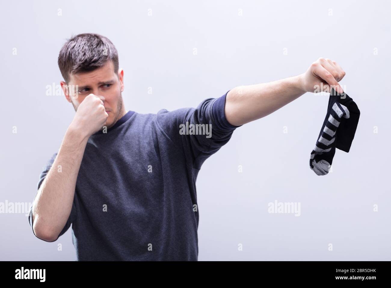 Young Man Holding His Stinking Socks Against White Background Stock ...