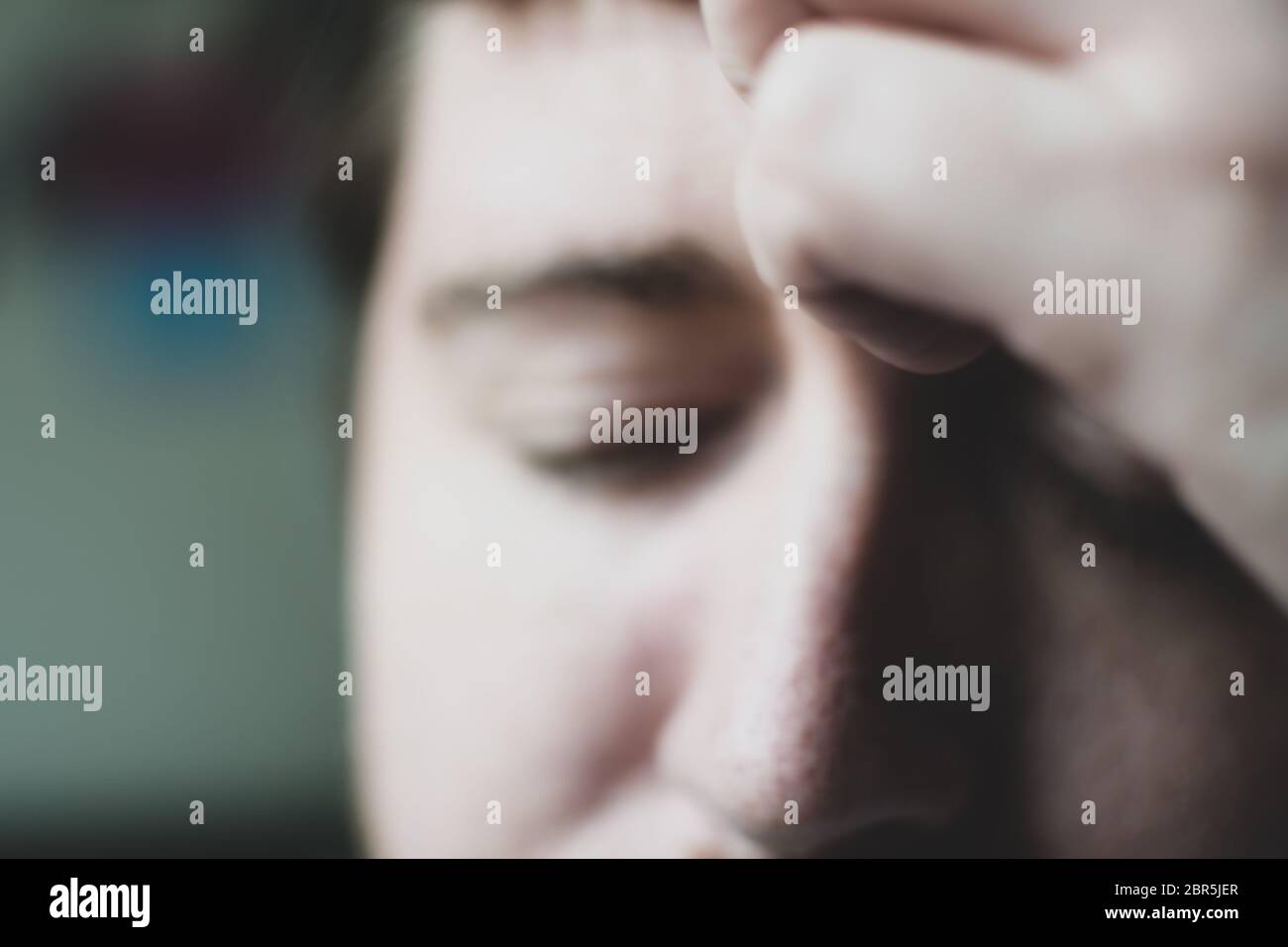 Out of focus male face with hand on head in cold light indicating ...