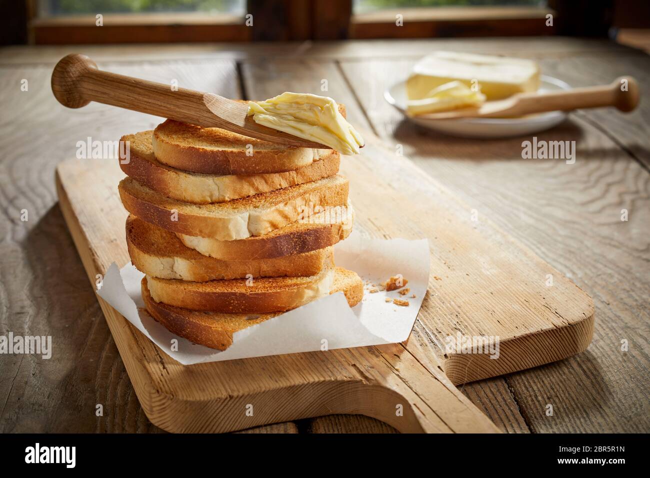Stack of golden crispy toast on a wooden chopping board with butter and ...