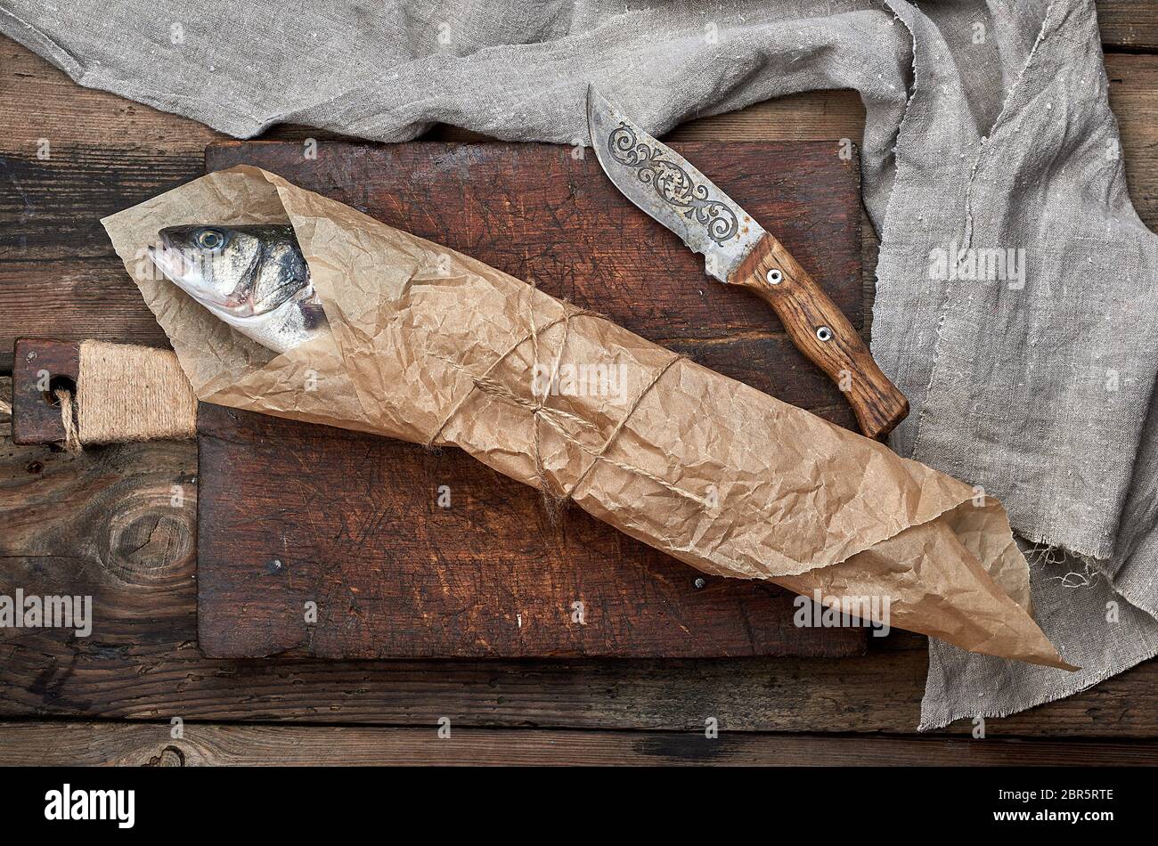 Fresh whole sea bass fish wrapped in a brown paper and tied with a rope ...