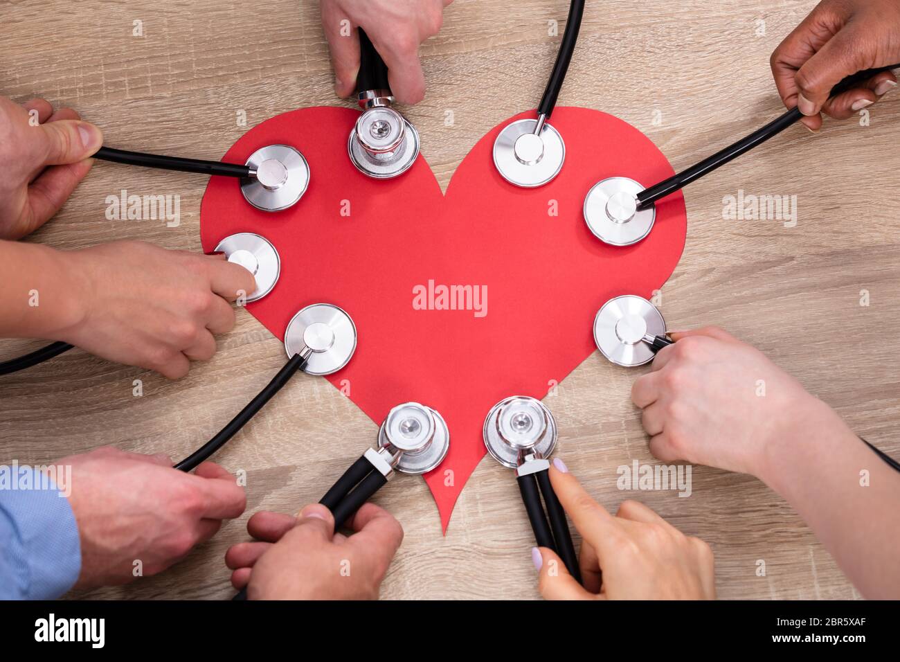 Group Of People's Hand Checking Red Heart With Stethoscope Above Wooden ...