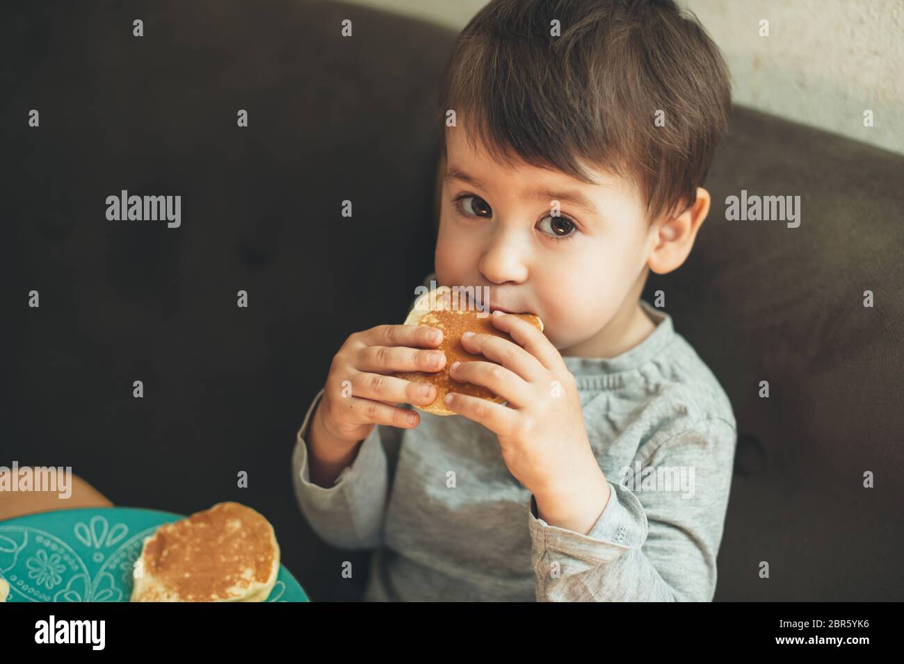 Caucasian boy looking up o camera while eating delicious cakes at home ...