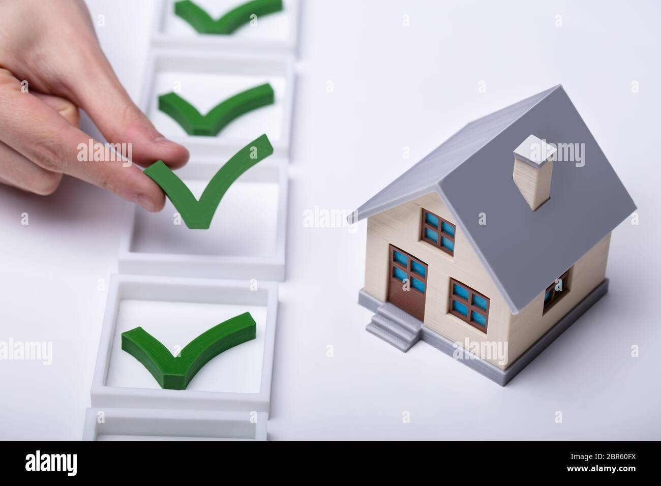 Person's Hand Placing Check Mark Sign Near The House Model On Desk ...