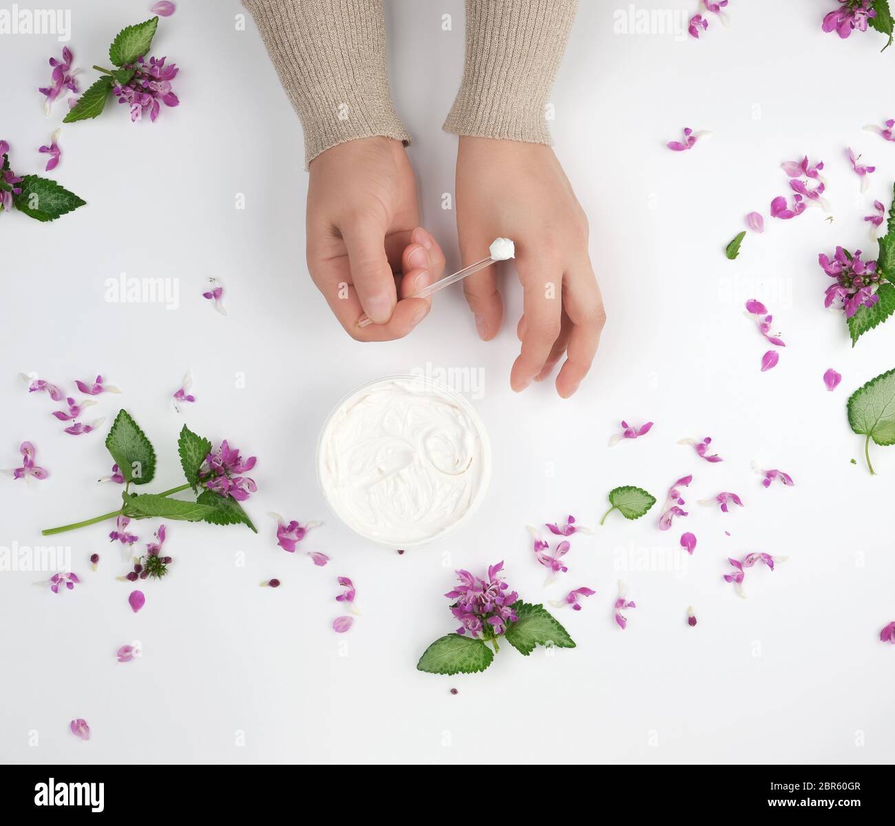two female hands and a jar with thick cream and pink flowers with green ...