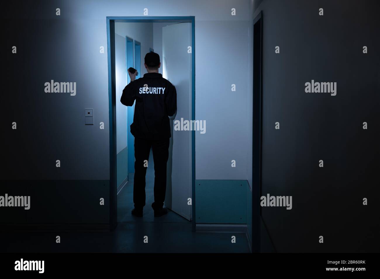 Rear View Of Male Security Guard With Flashlight Standing In Corridor ...