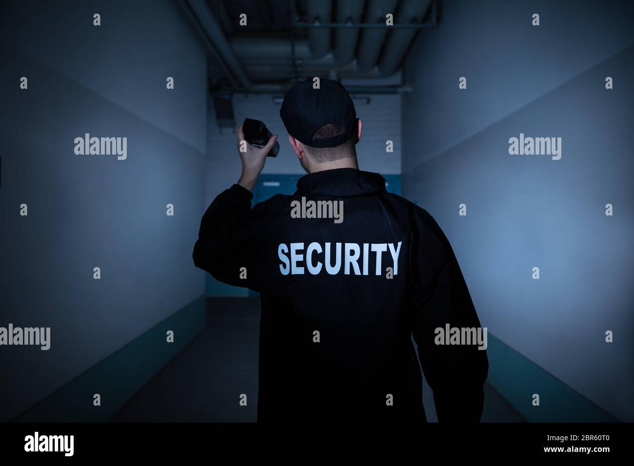 Rear View Of A Male Security Guard With Flashlight Standing In Corridor ...