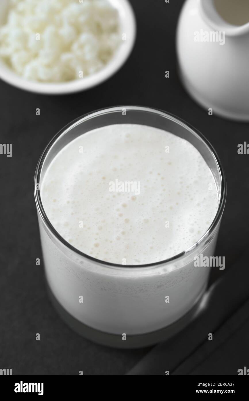 Fresh homemade kefir drink in glass, kefir grains and milk in the back ...