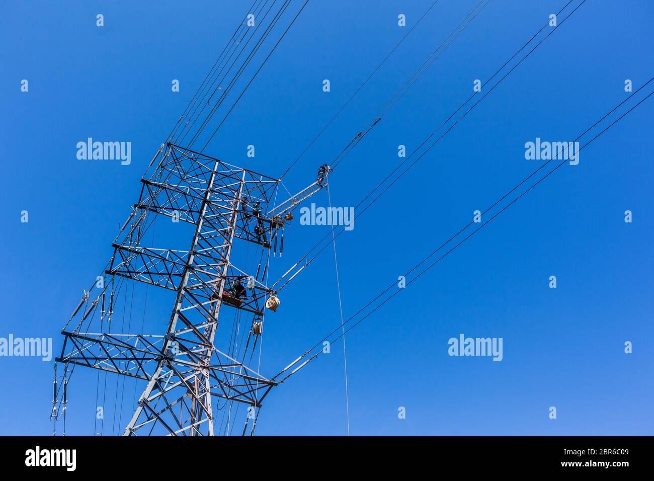 Electricians high up suspended on electrical steel tower installing new ...
