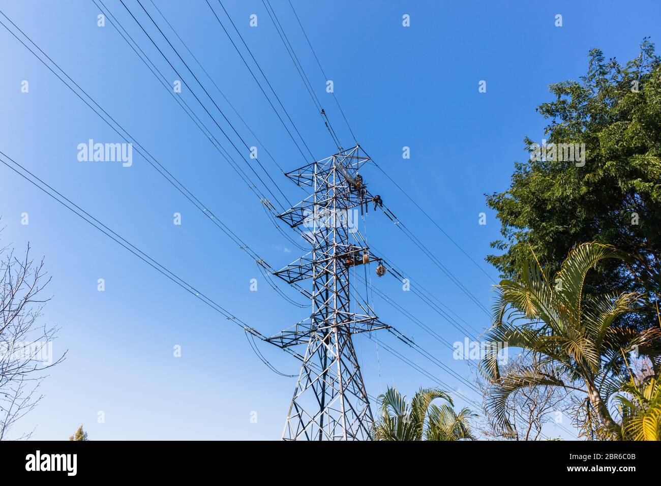 Electricians high up suspended on electrical steel tower installing new ...