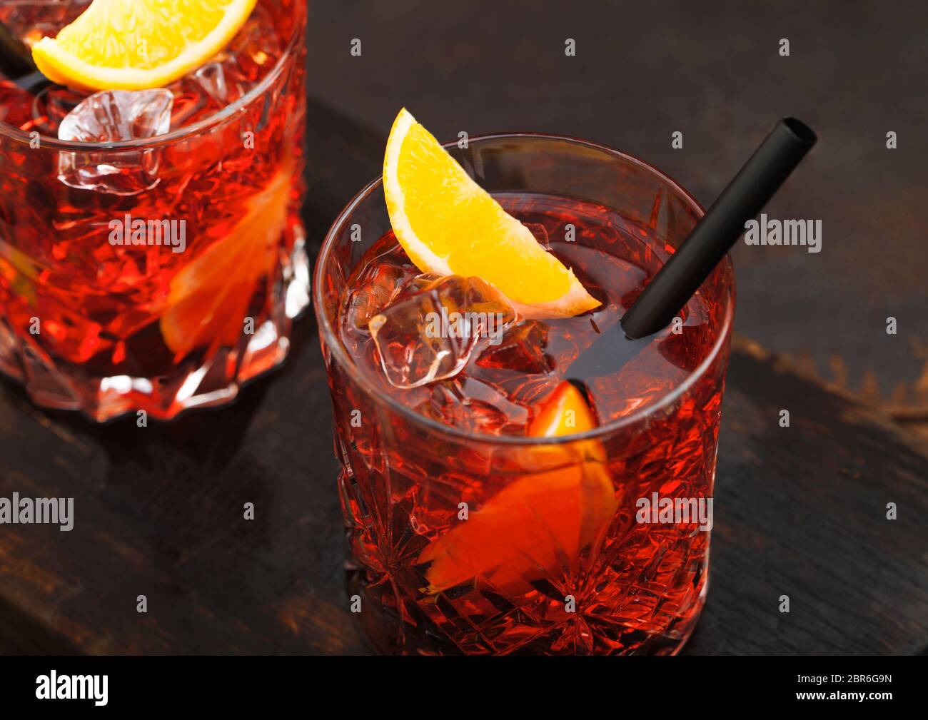 Negroni cocktail in crystal glasses with orange slice and black straw ...
