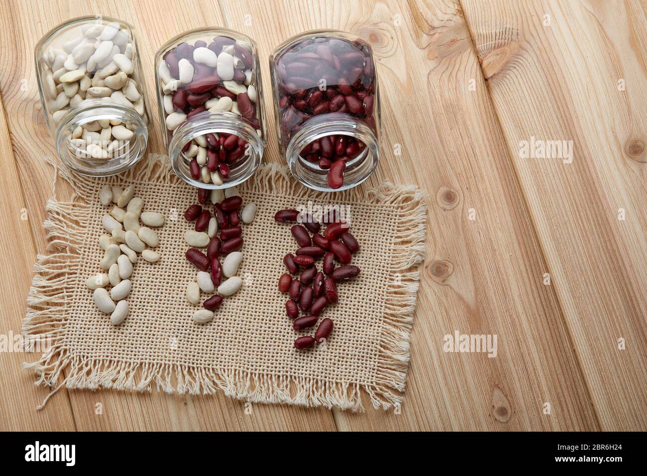 Various types of dry haricots in glass jars lying on wooden background ...