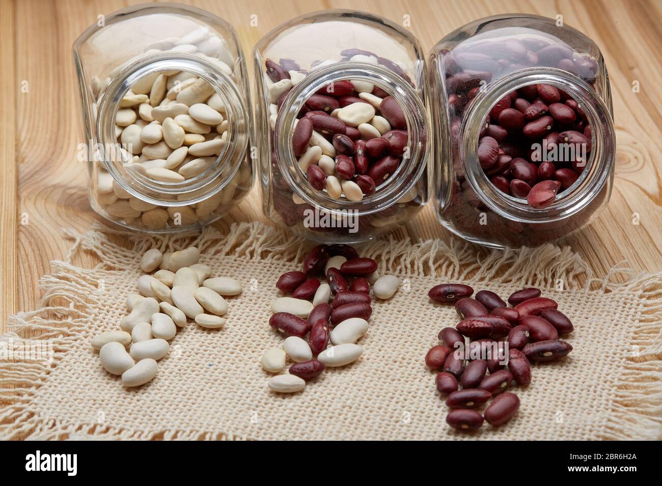 Various types of dry haricots in glass jars lying on wooden background ...