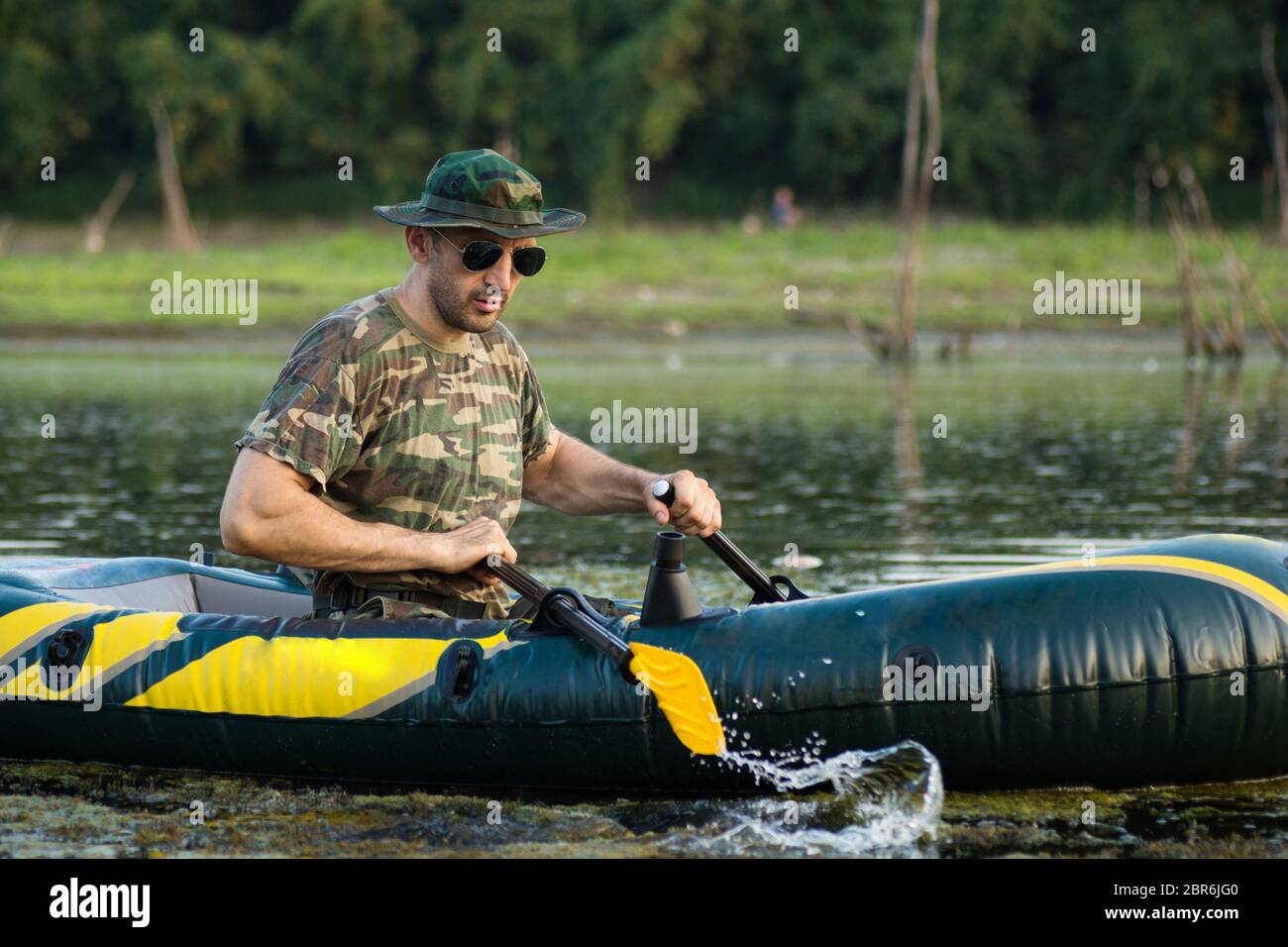 The oarsman is rowing in inflatable boat on the shallow lake for ...