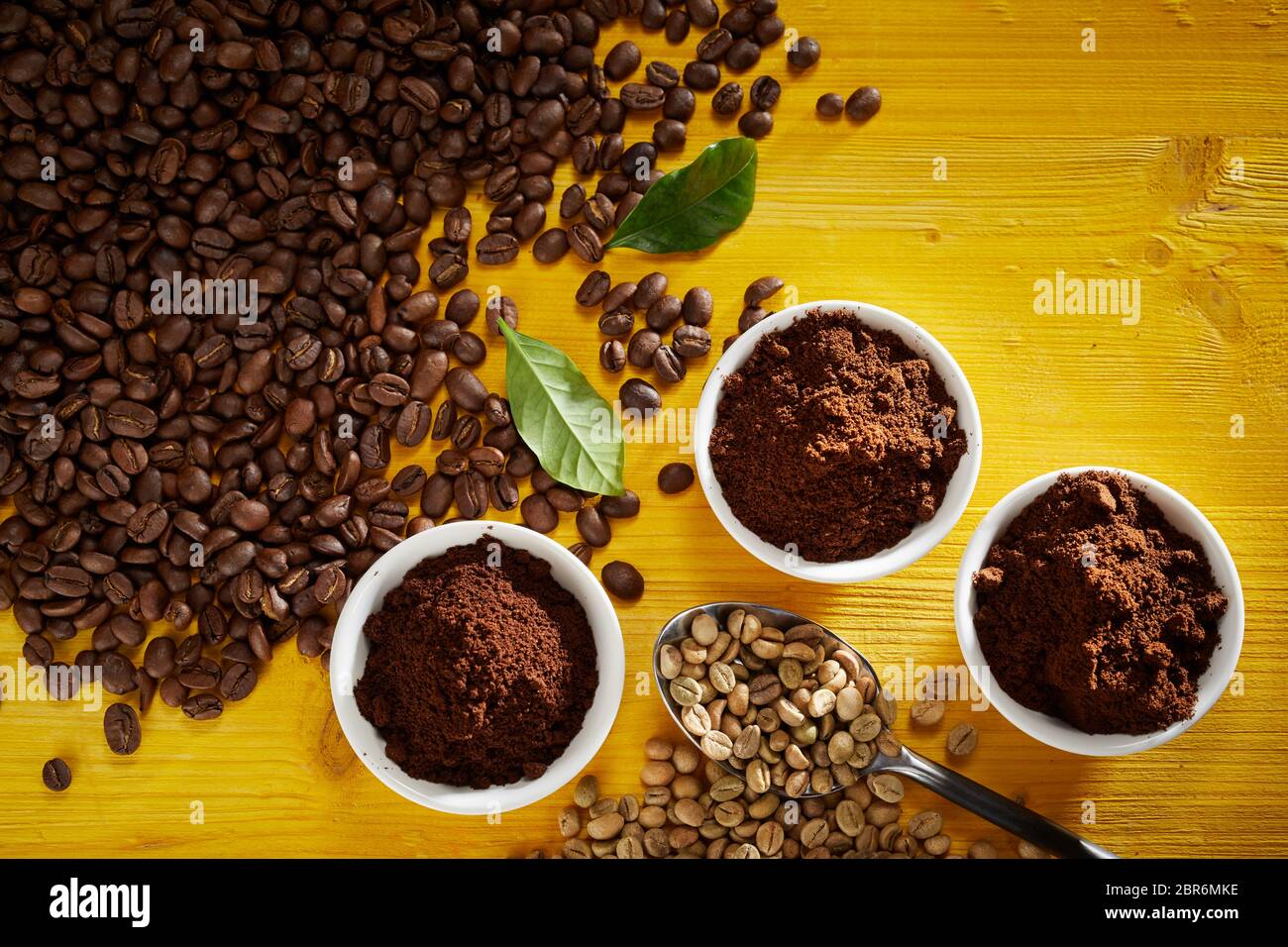 Roasted and raw coffee beans with fresh grounds in small bowls viewed ...