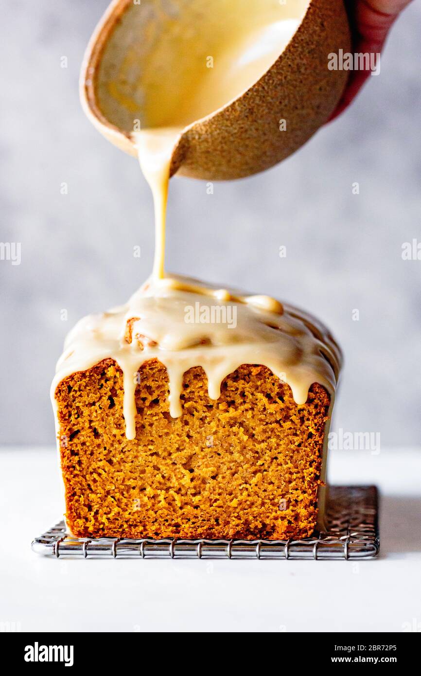 Maple icing in a hand held bowl poured over a loaf of pumpkin bread ...
