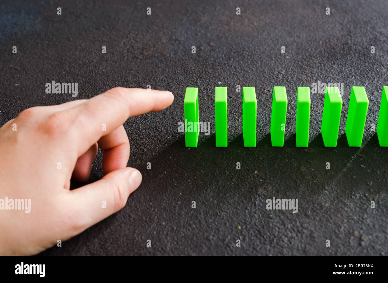 Hand ready to push domino piece to cause chain reaction. Row of green ...
