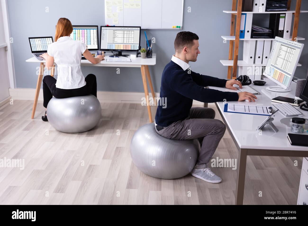 Two Businesspeople Working On Computer In Office Sitting On Fitness ...