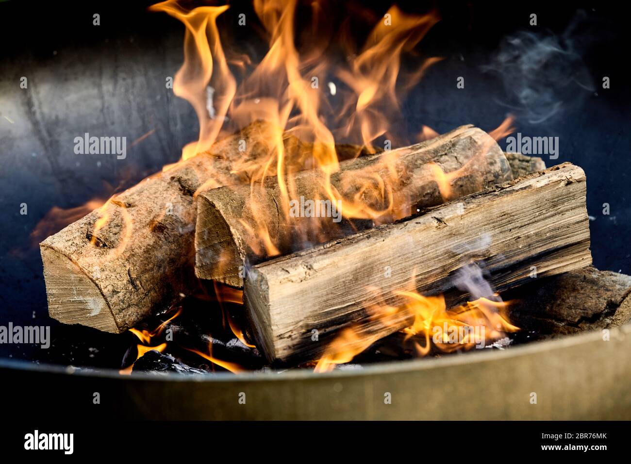 Burning logs flaming in a barbecue fire on a bed of hot coals in a ...