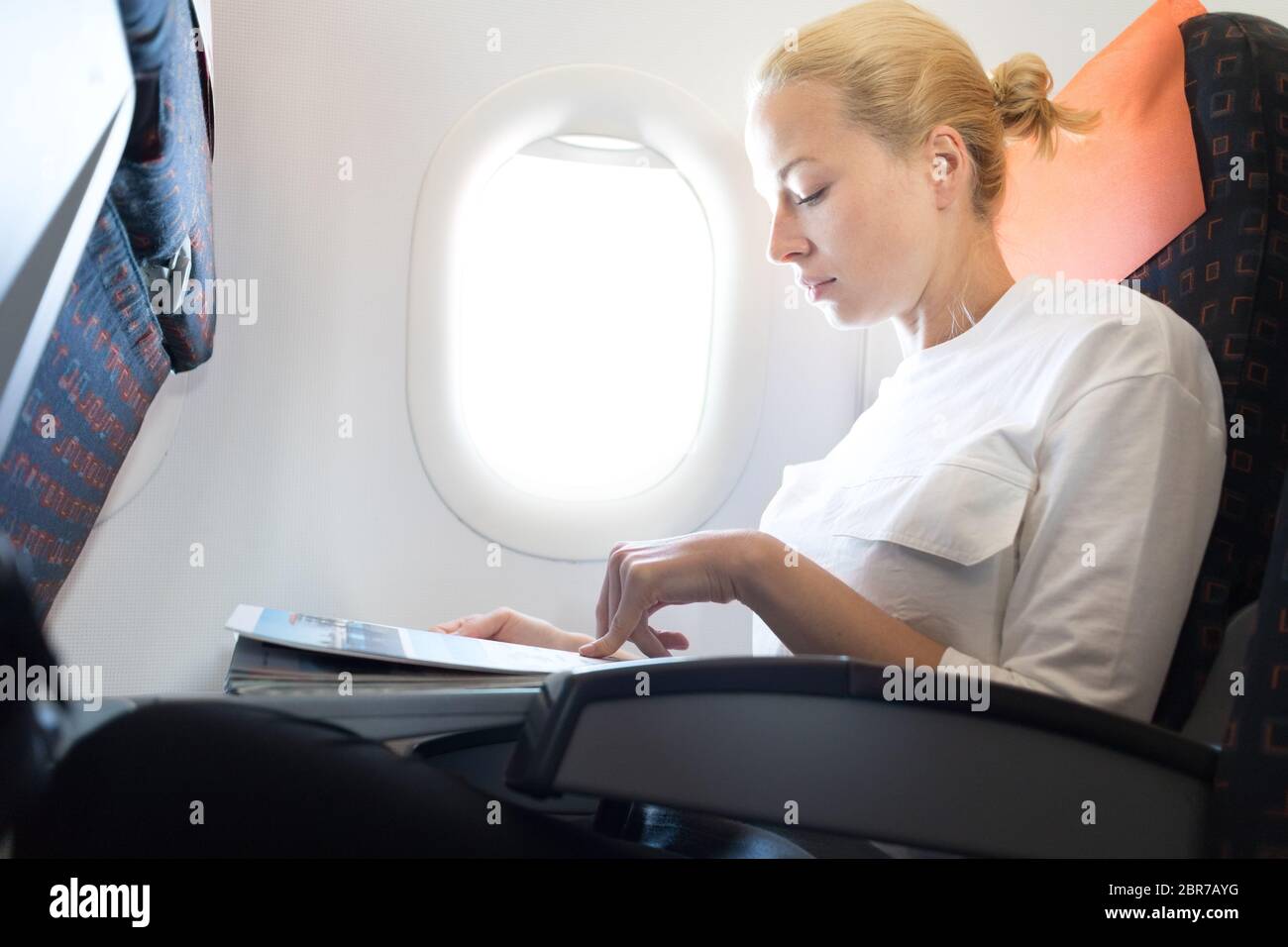 Woman reading in flight magazine on airplane. Female traveler reading ...