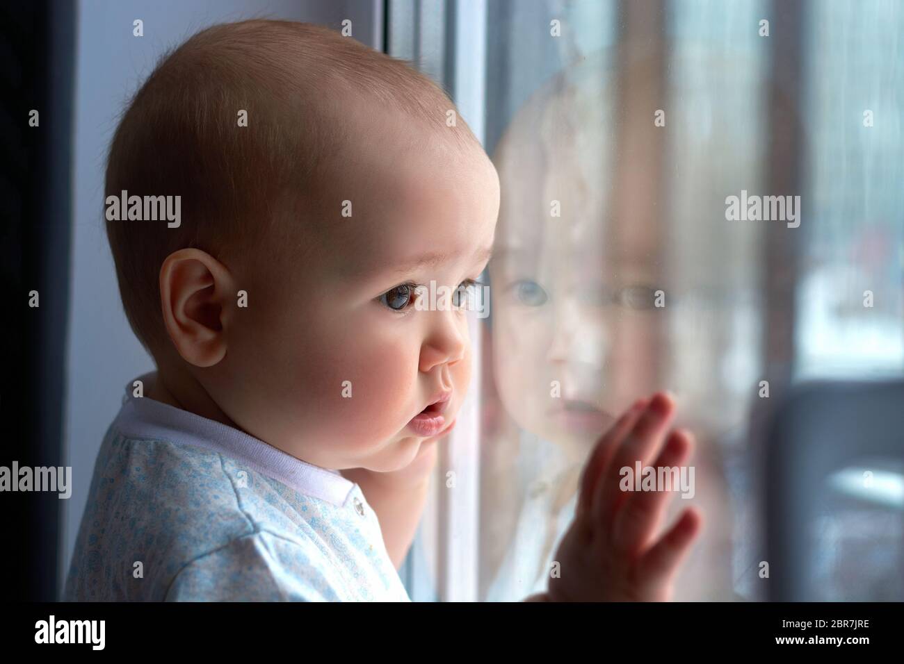 a small boy on the windowsill looks out the window.a child with a sad ...