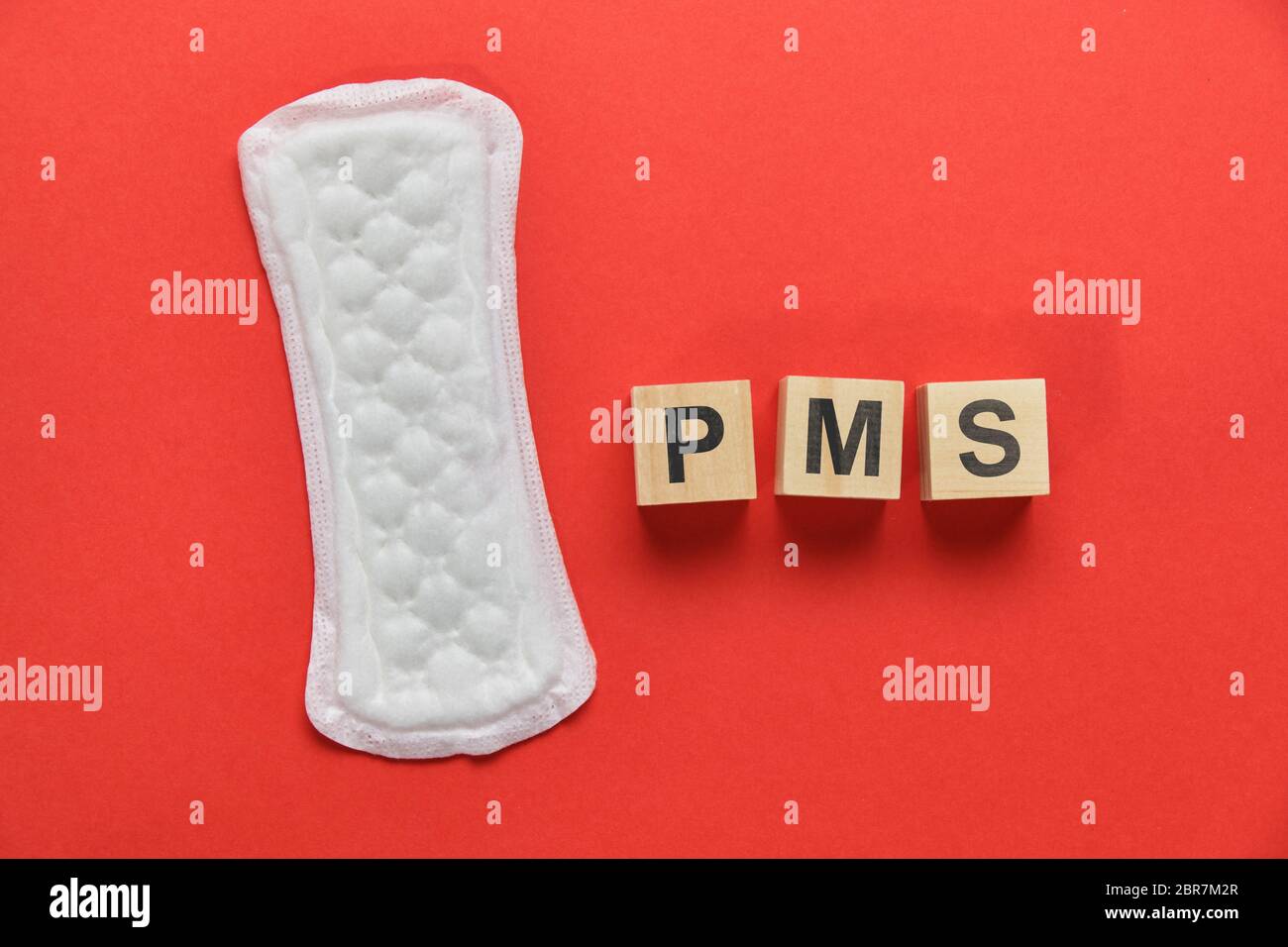 Female pad on a red background with the inscription PMS on wooden cubes ...