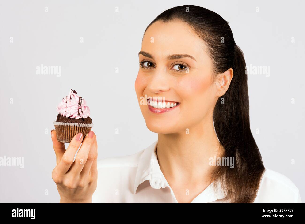 The beautiful woman is holding and eating bright pink cupcake dessert ...