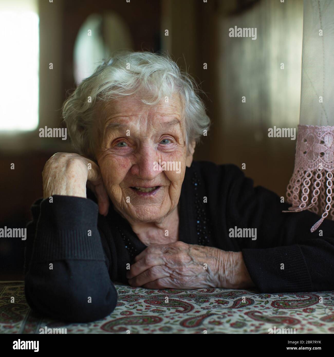 Portrait of a retired old woman sitting at a table Stock Photo - Alamy