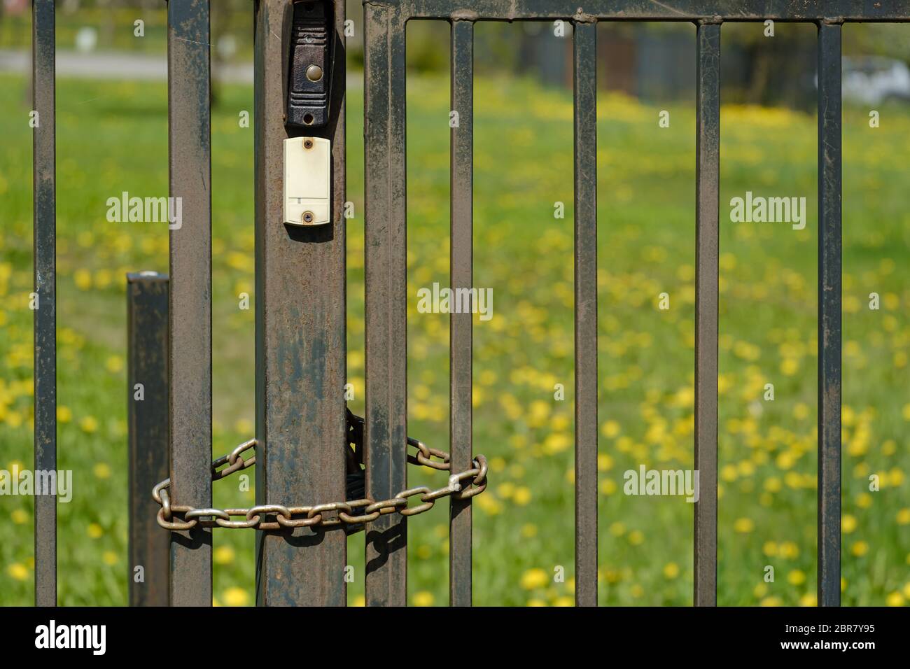 Metal gate with a bell closed on a chain and a lock, on a blurry ...