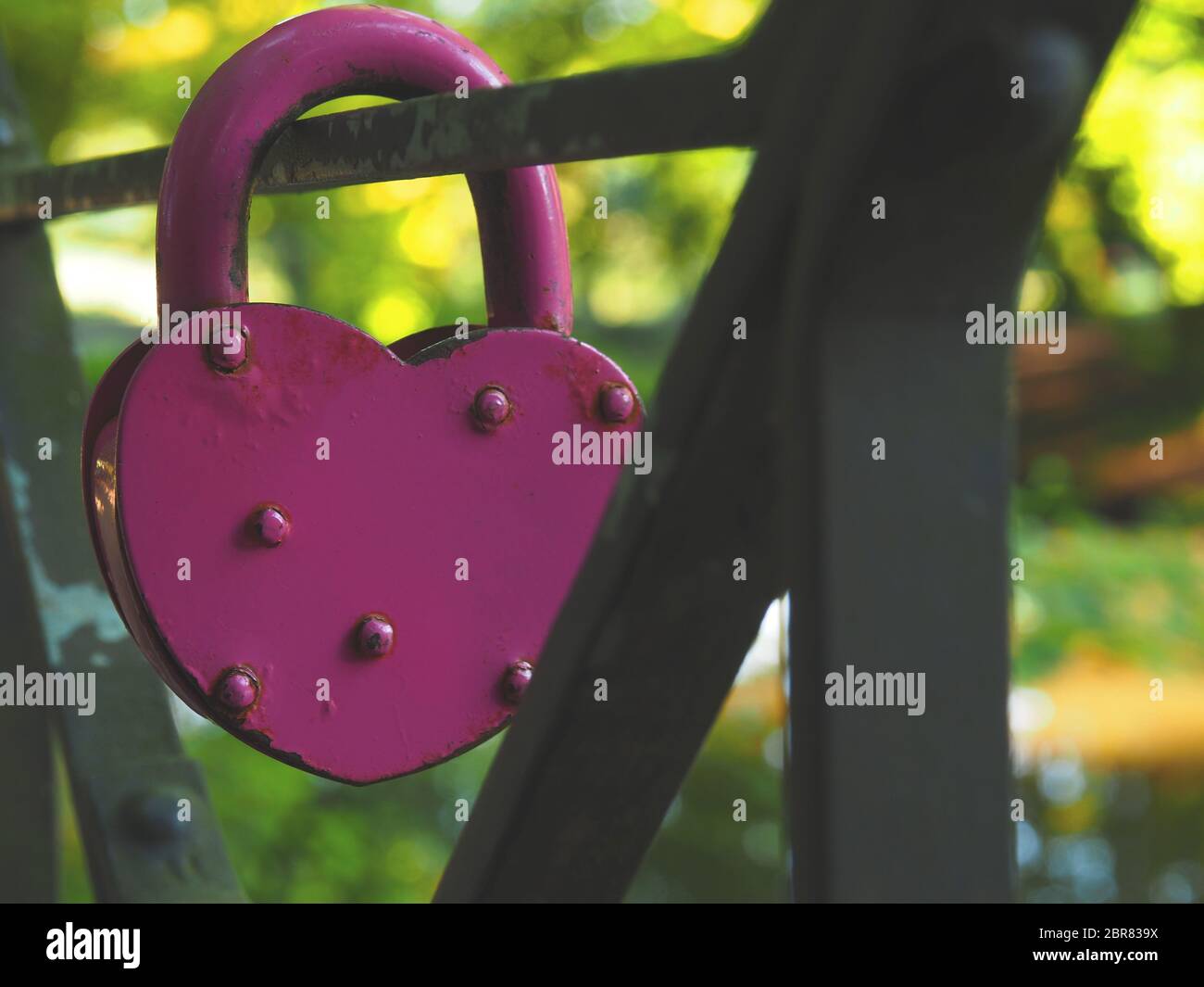 Old rusty pink heart shaped padlock on a steel bridge, close up shot ...