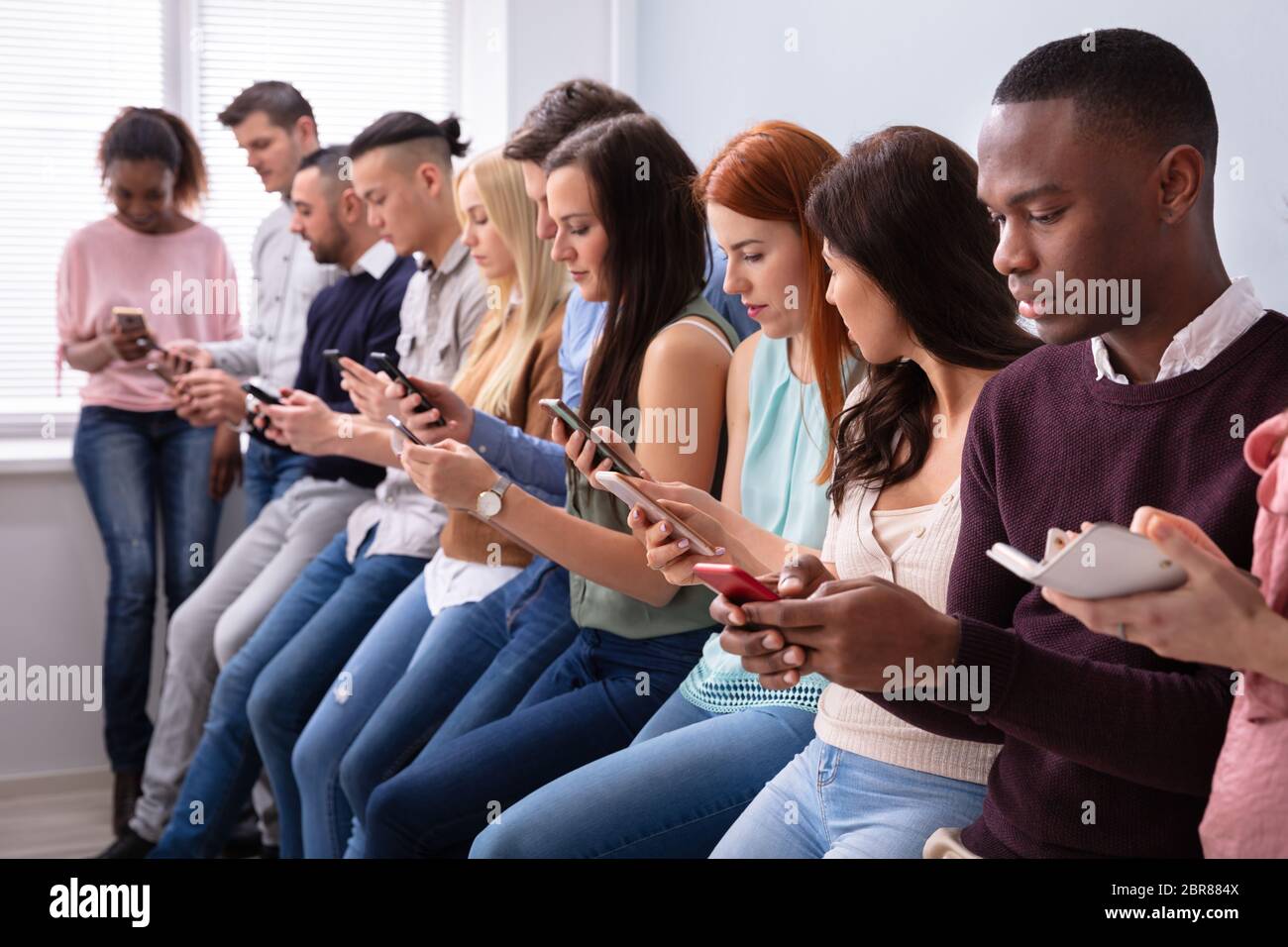Multi-ethnic Young People Leaning Near Table In Row Using Smartphone ...