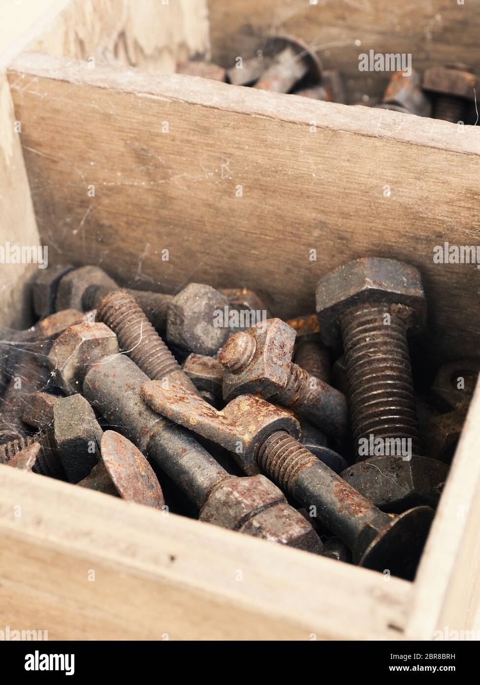 Rusty old nuts and bolts in a rustic wooden box on a workbench ...