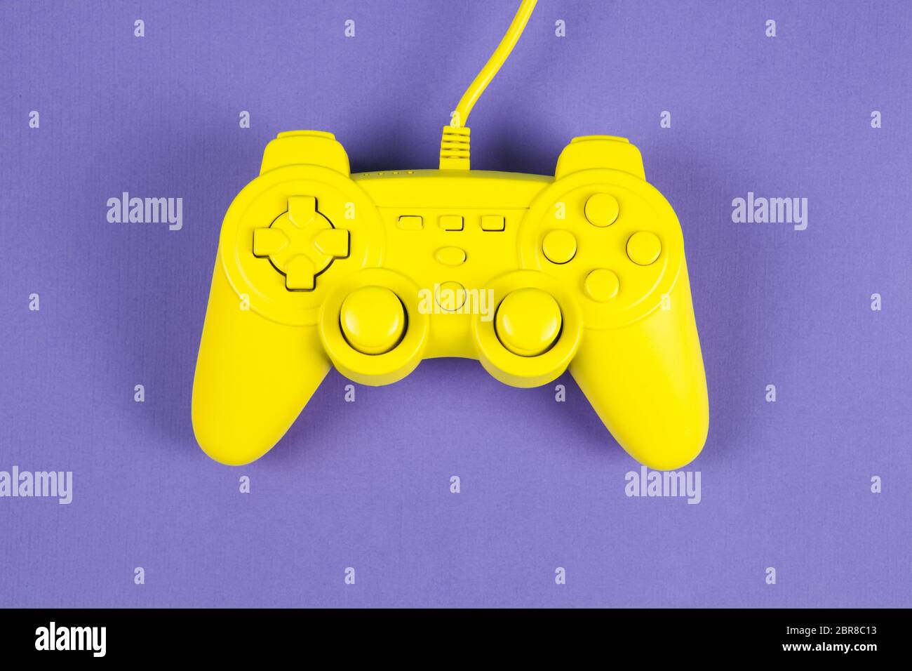 a yellow painted video game controller on a plain purple background ...