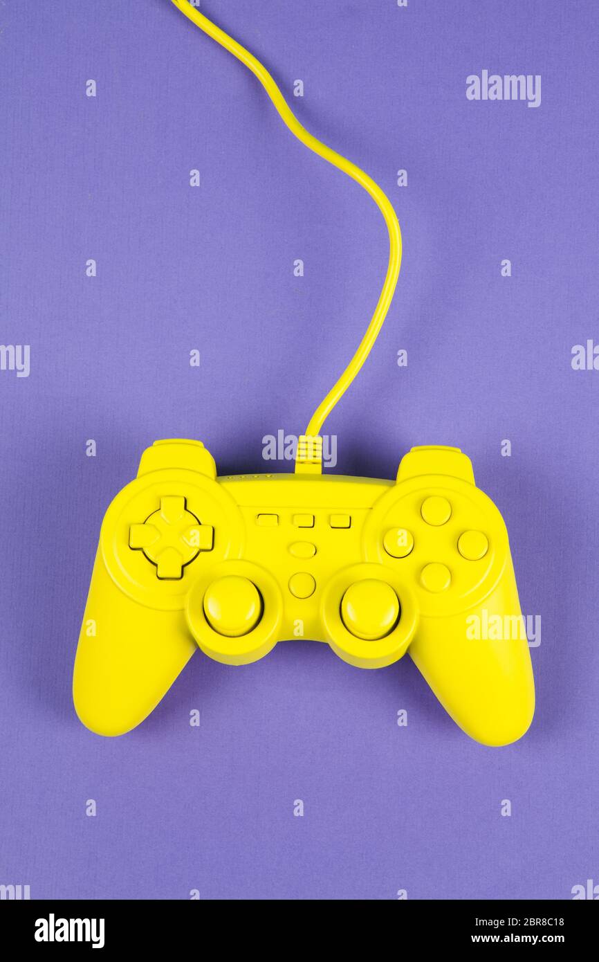 a yellow painted video game controller on a plain purple background ...