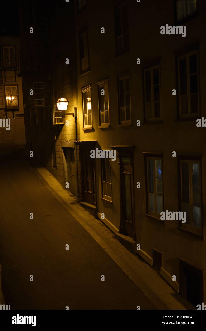 A street lamp lights up a dark narrow steep street at night in the ...