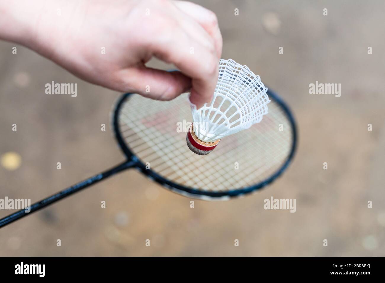 hand holds shuttlecock over badminton racquet on outdoor earth ground ...