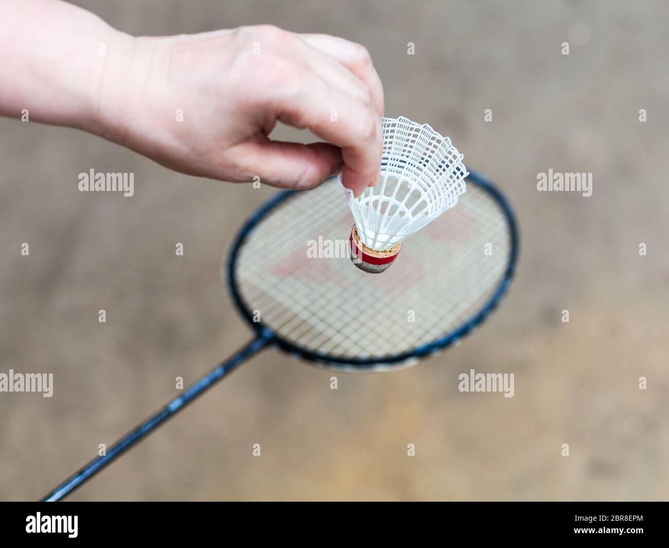 hand holds white shuttlecock over badminton racquet on outdoor earth ...