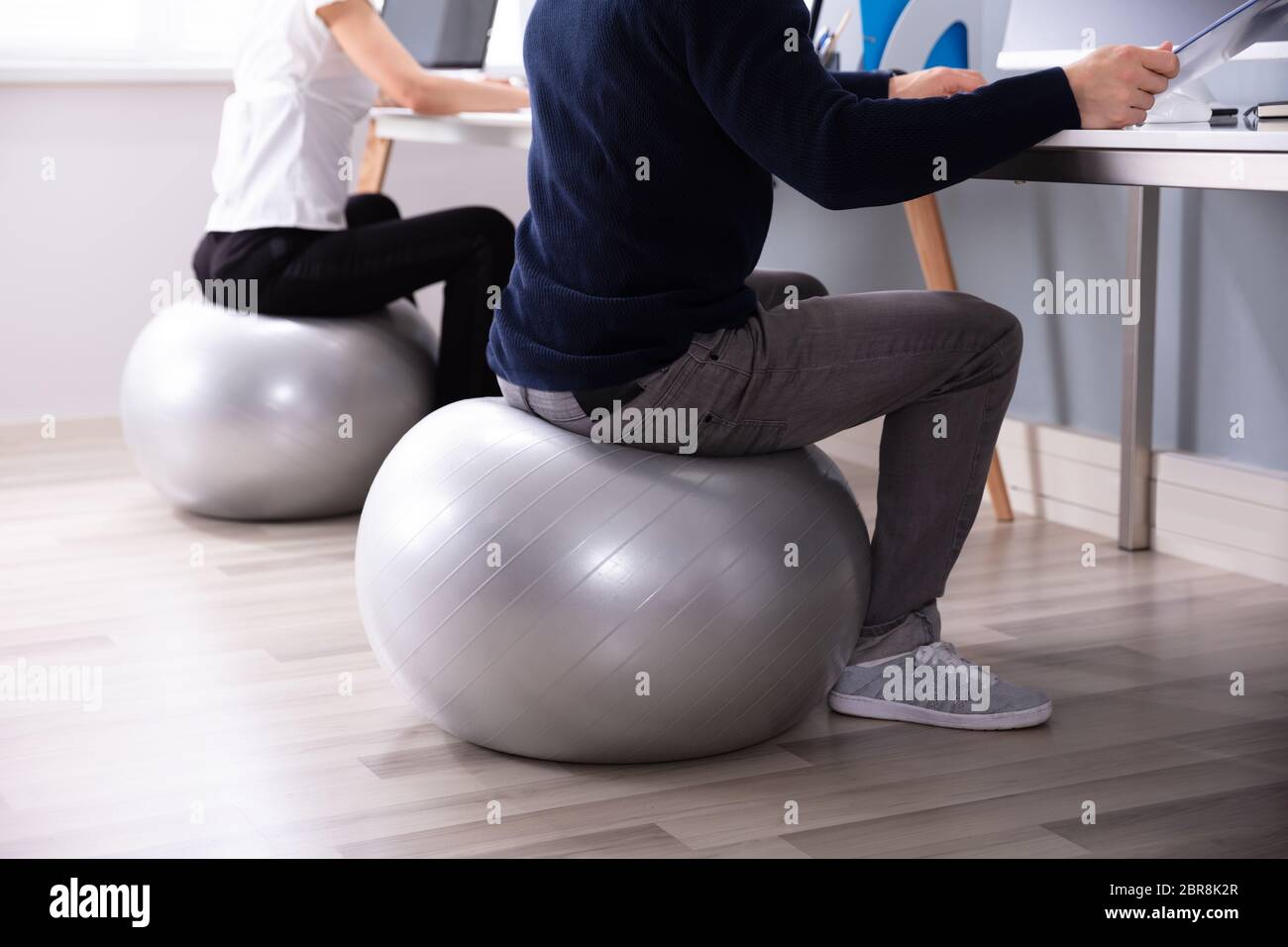 Two Businesspeople Working On Computer In Office Sitting On Fitness ...