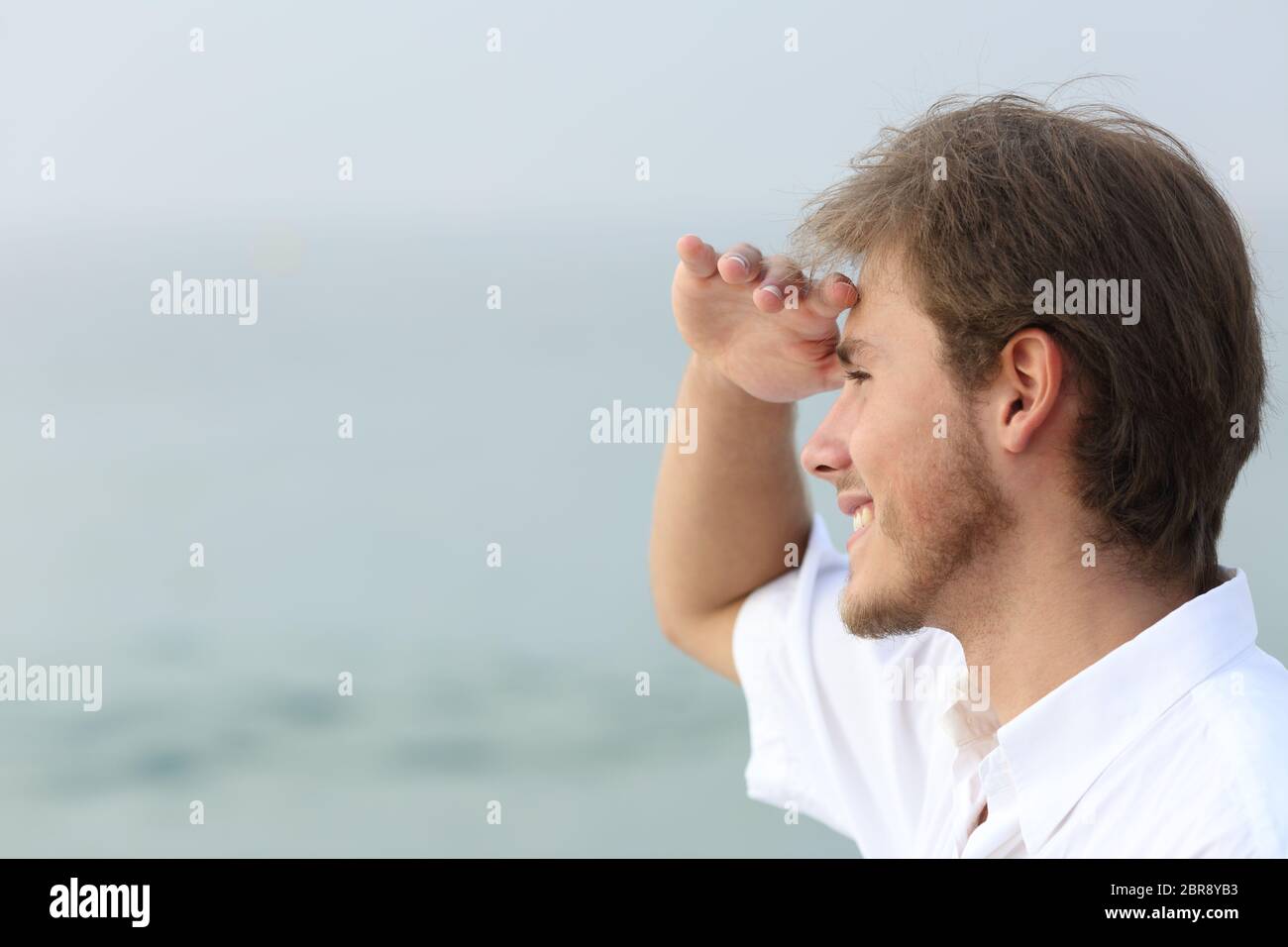 Happy man scouting looking away on the beach with hand on forehead ...