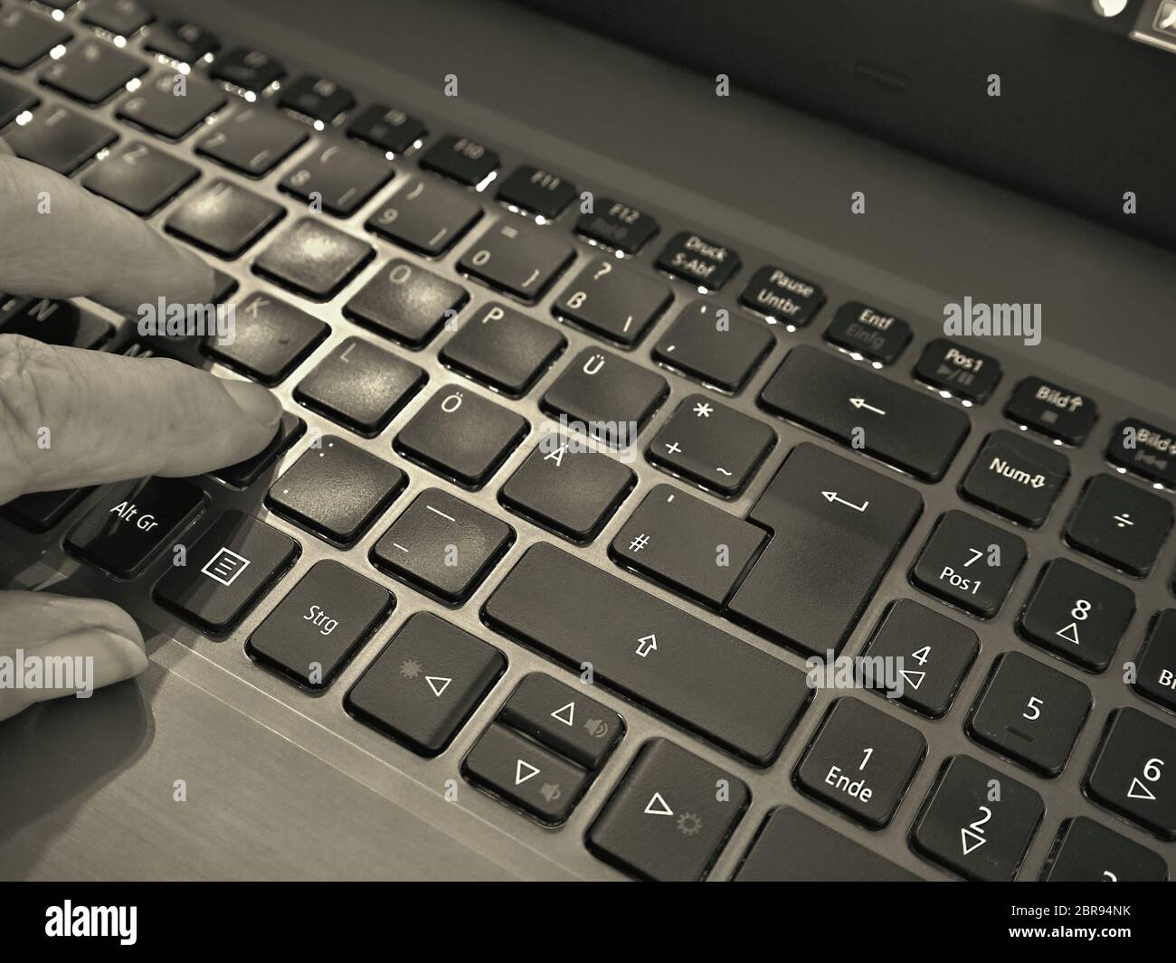 A lighted laptop keyboard, on the left side you can see three fingers ...