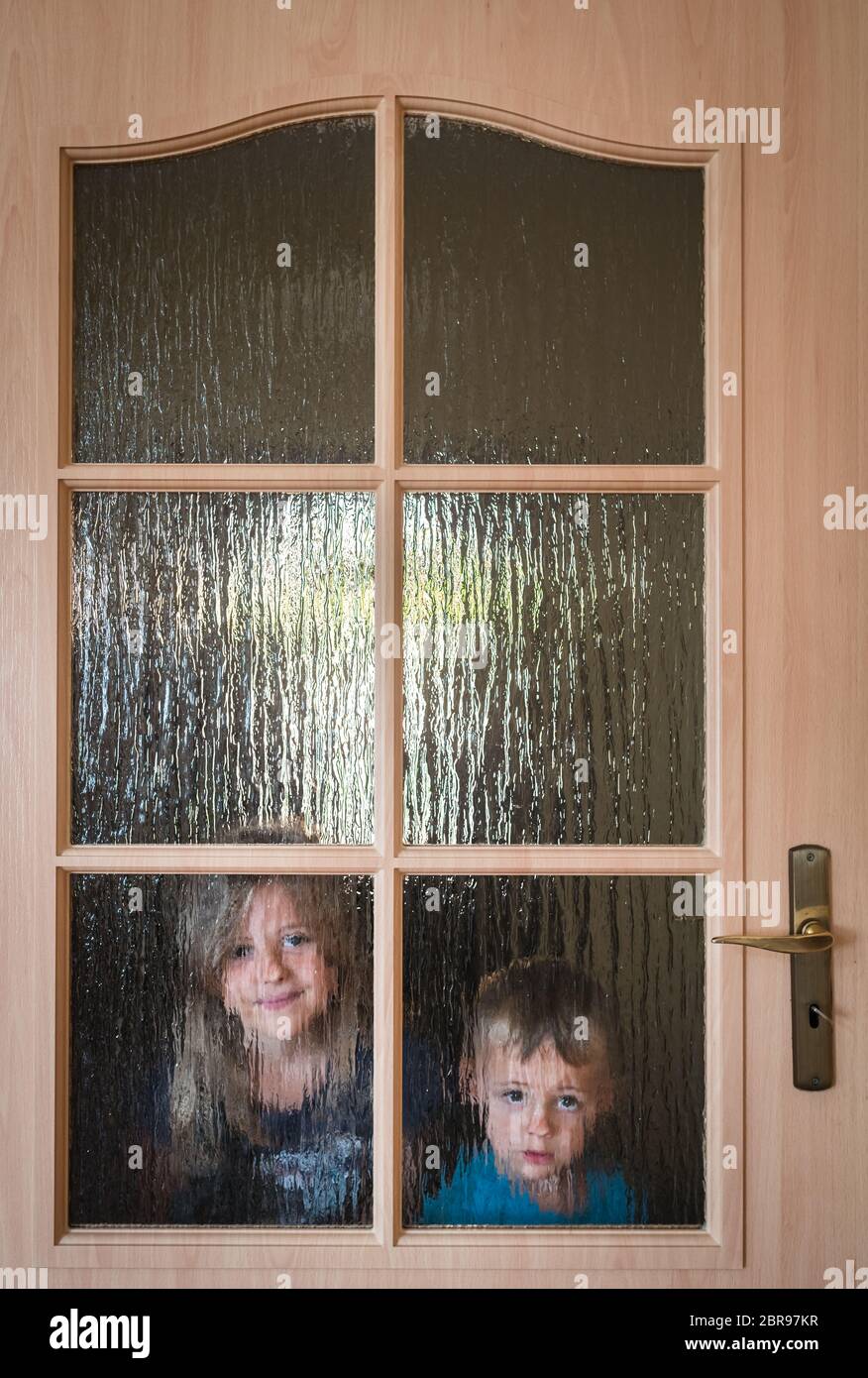 Portrait of a cute little Caucasian boy and girl hiding behind a door ...