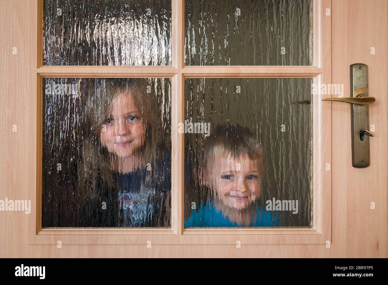 Portrait of a cute little Caucasian boy and girl hiding behind a door ...