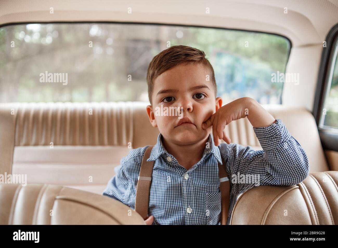Caucasian little boy in vintage clothes sitting inside a retro car ...