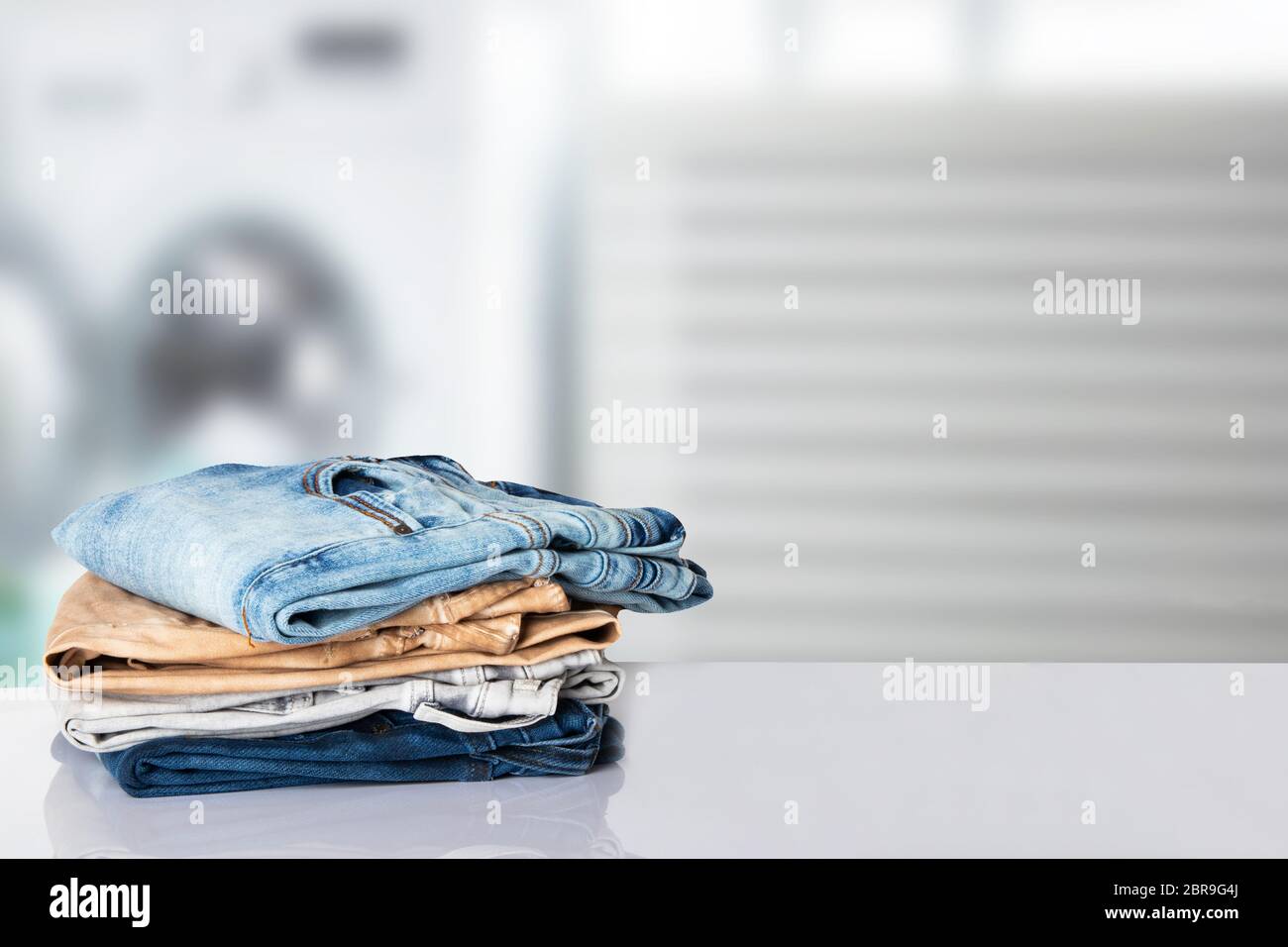 Stack of jeans clothes. Pile of colorful jeans on white table with ...