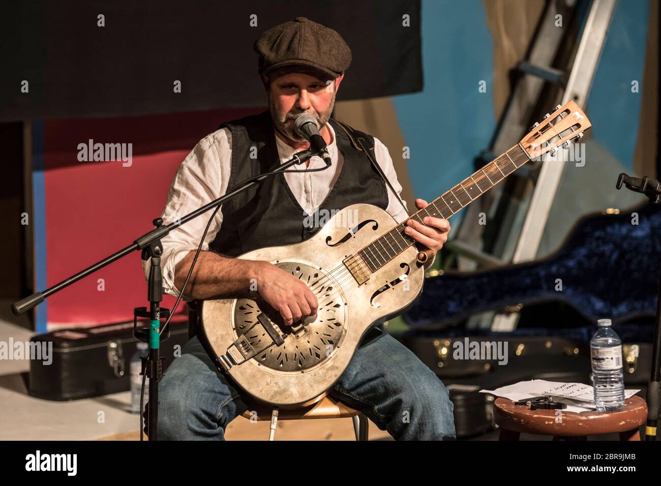 Male folk singer, sitting as he sings and plays resonator guitar, in ...