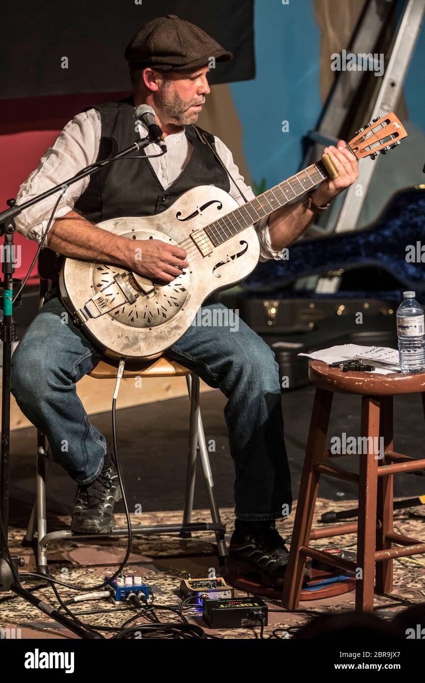 Male folk singer, sitting as he sings and plays resonator guitar, in ...