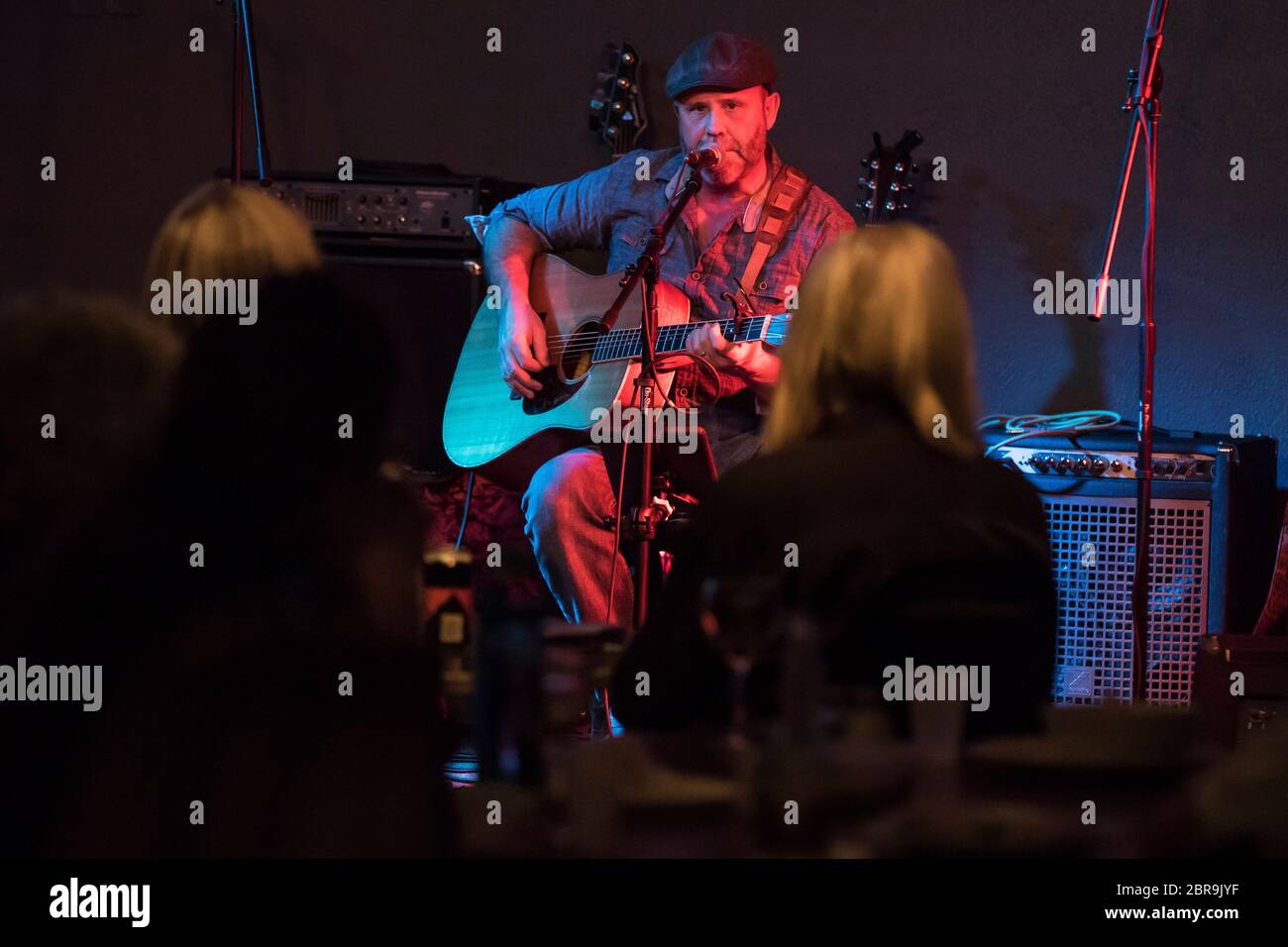 Male folk singer, sitting as he sings and plays guitar, in indoor ...