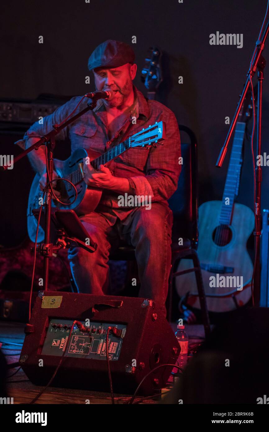 Male folk singer, sitting as he sings and plays resonator guitar, in ...
