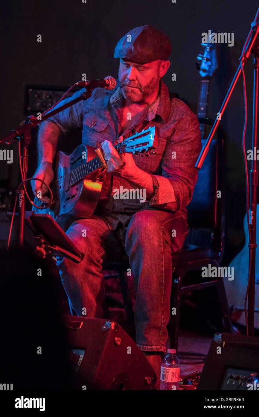 Male folk singer, sitting as he sings and plays resonator guitar, in ...