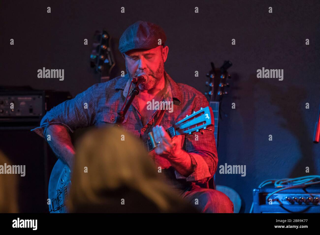 Male folk singer, sitting as he sings and plays resonator guitar, in ...